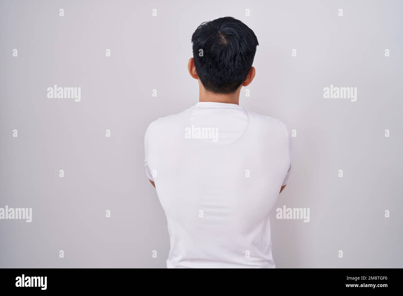 Young asian man standing over white background standing backwards ...