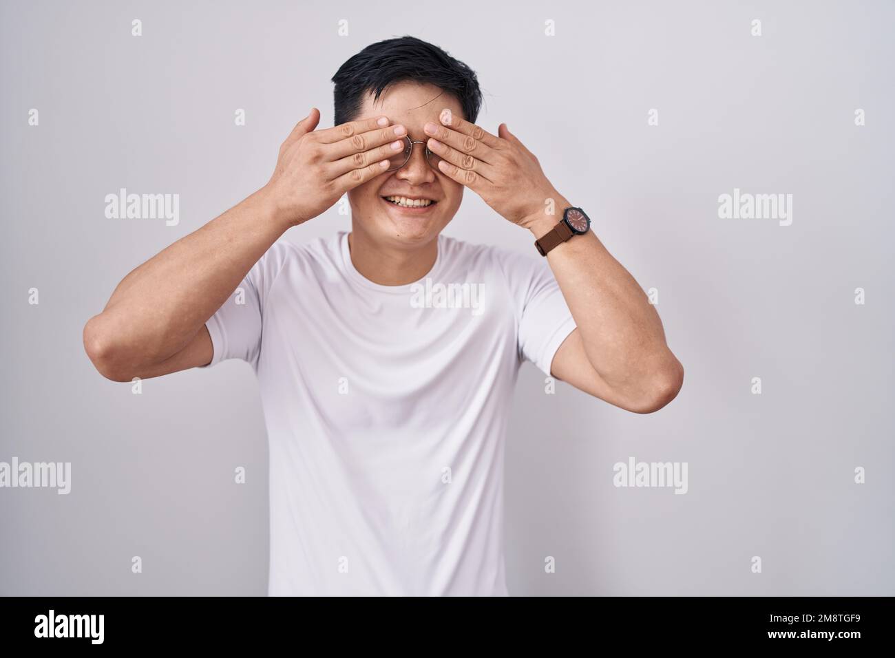 Young asian man standing over white background covering eyes with hands ...
