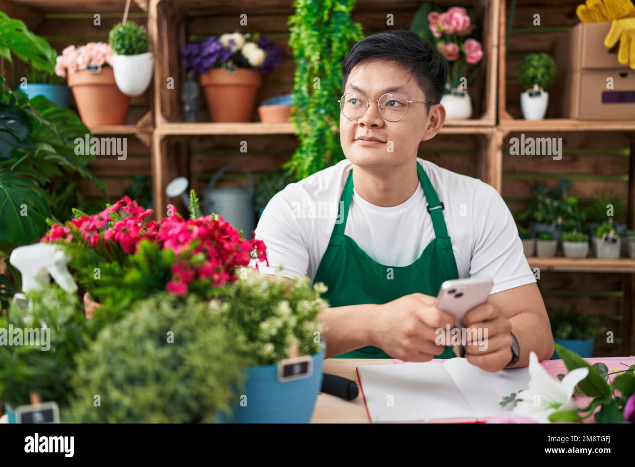 Young chinese man florist smiling confident using smartphone at flower ...