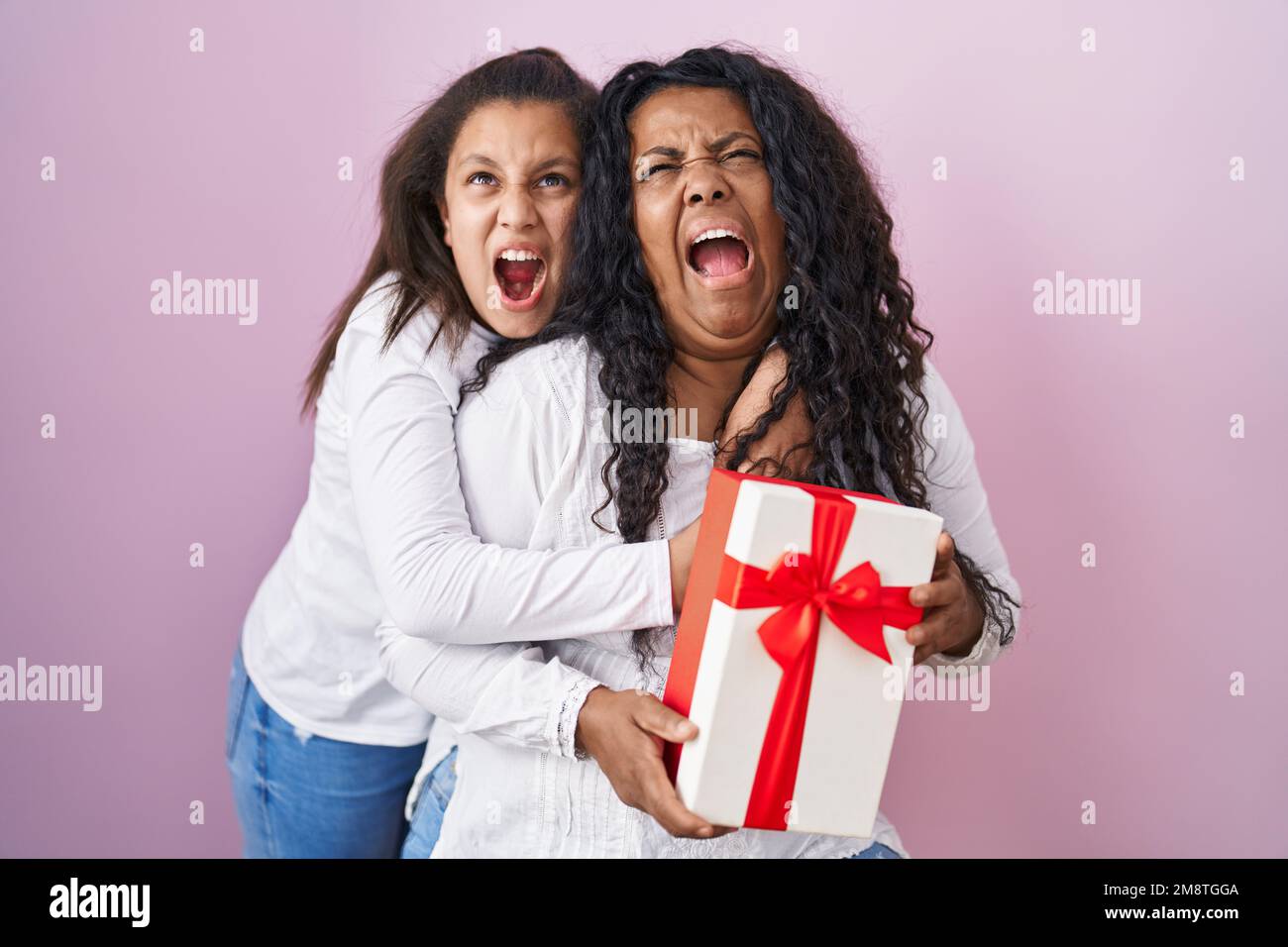 Mother and young daughter holding with presents angry and mad screaming ...