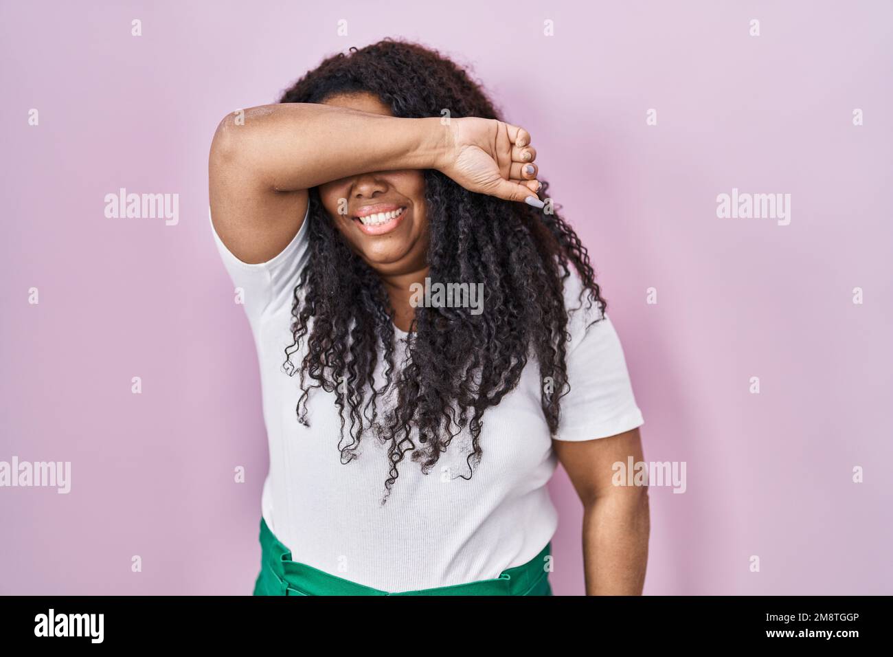 Plus size hispanic woman standing over pink background covering eyes ...