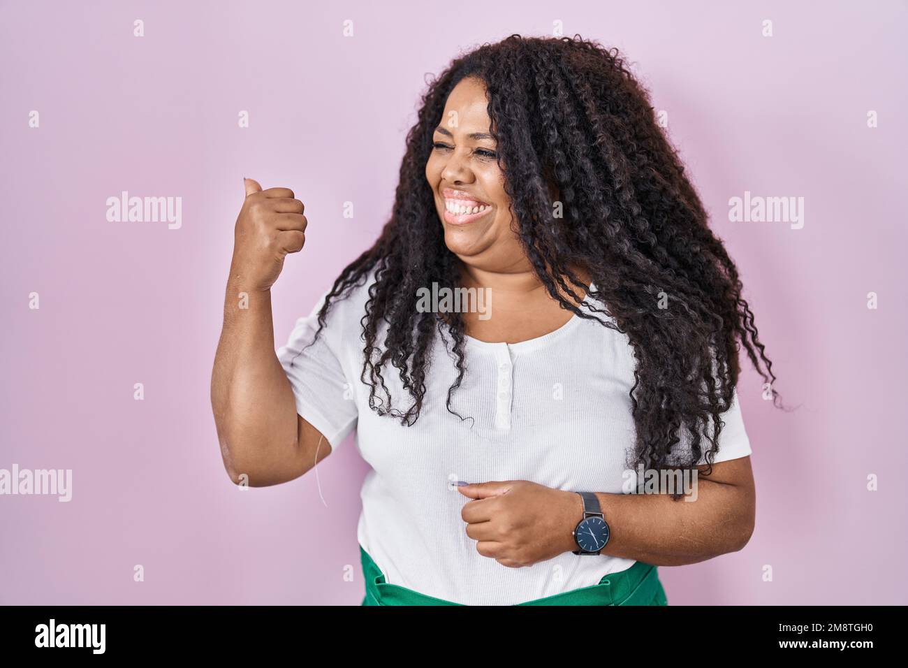 Plus size hispanic woman standing over pink background smiling with ...
