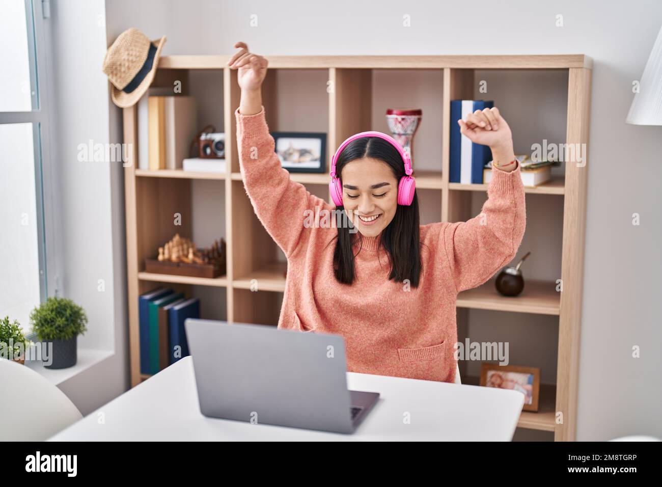 Young hispanic woman listening to music and dancing sitting on table at ...