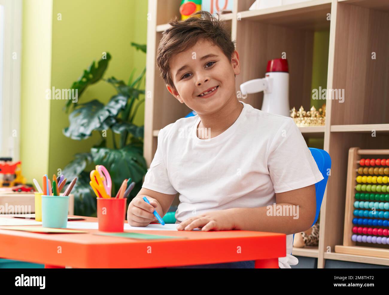 Adorable hispanic boy preschool student sitting on table drawing on ...
