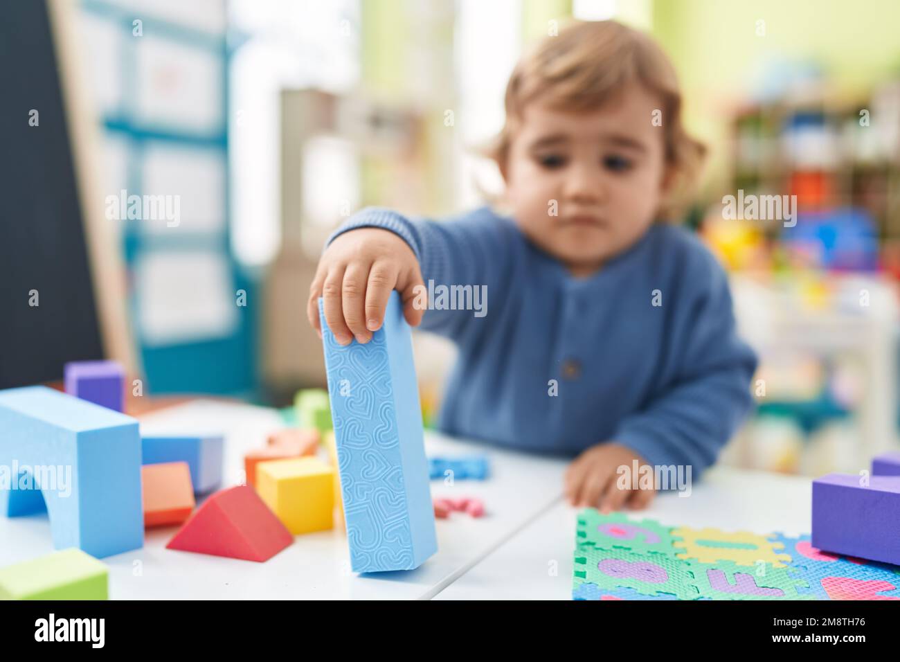 Adorable hispanic toddler playing with construction blocks standing at ...