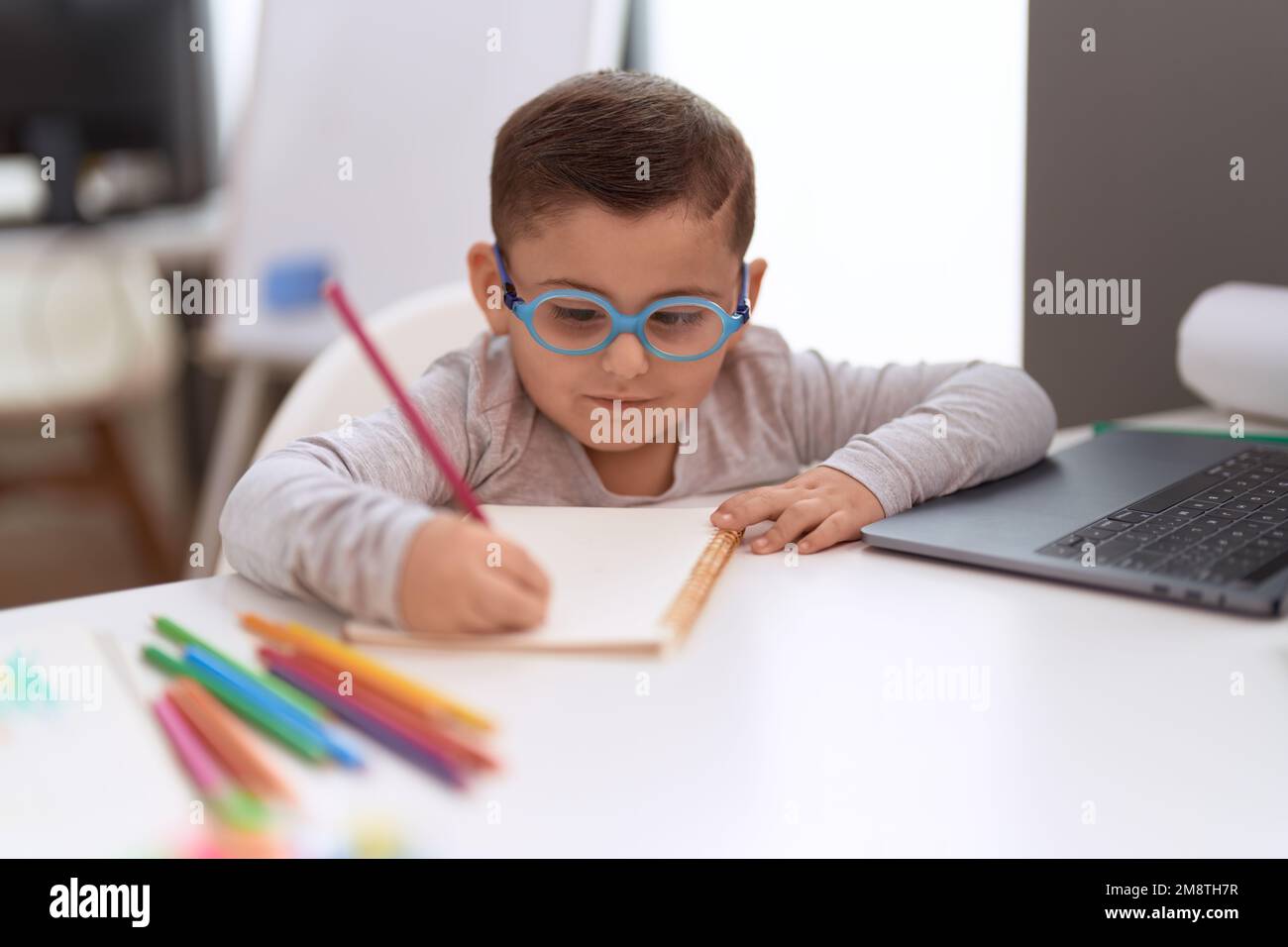 Adorable hispanic toddler student using laptop drawing on notebook at ...