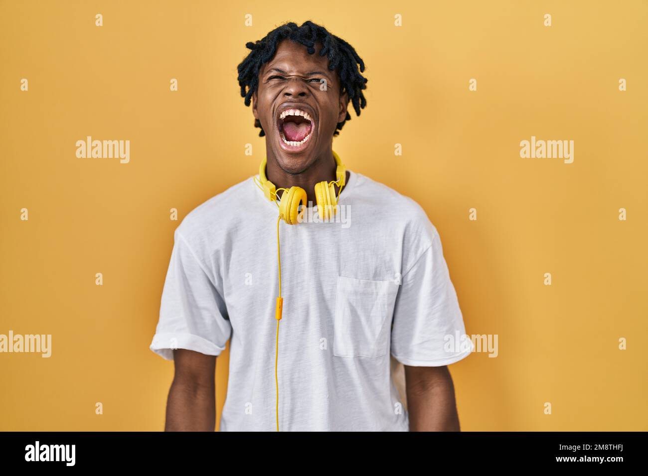 Young african man with dreadlocks standing over yellow background angry ...