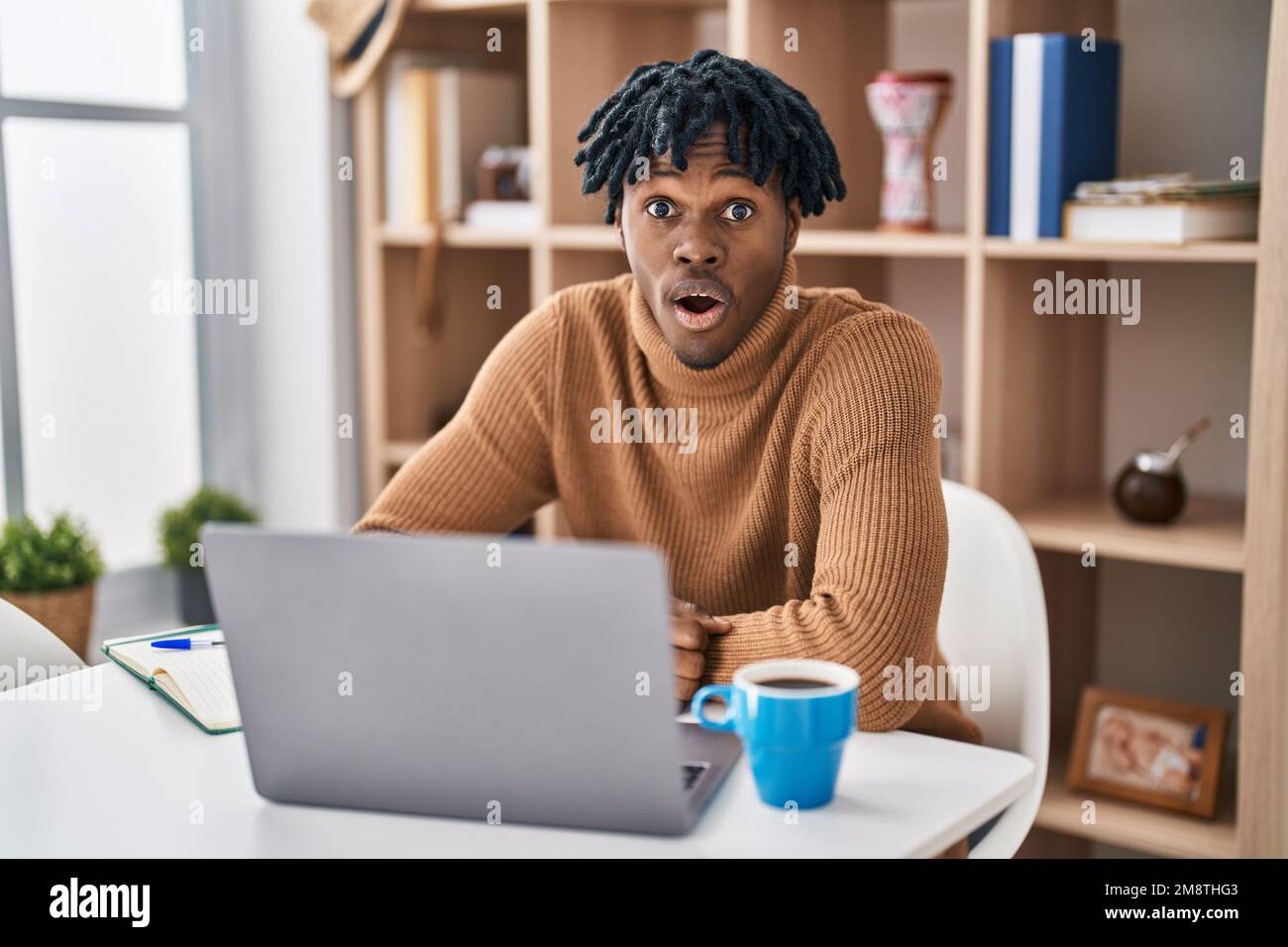 Young african man with dreadlocks working using computer laptop afraid ...