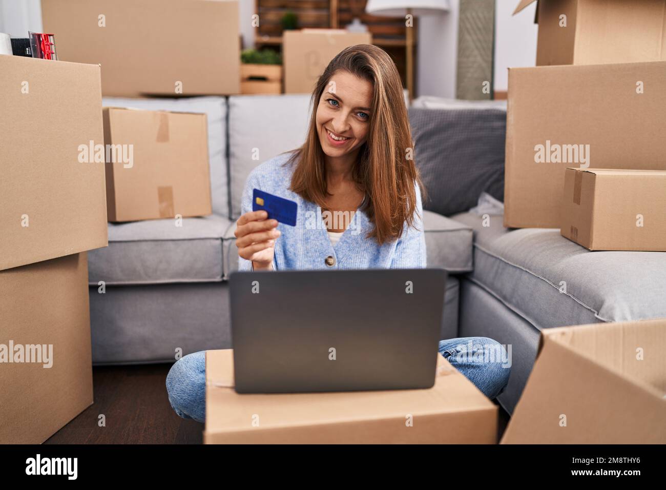 Young woman using laptop and credit card sitting on floor at new home ...