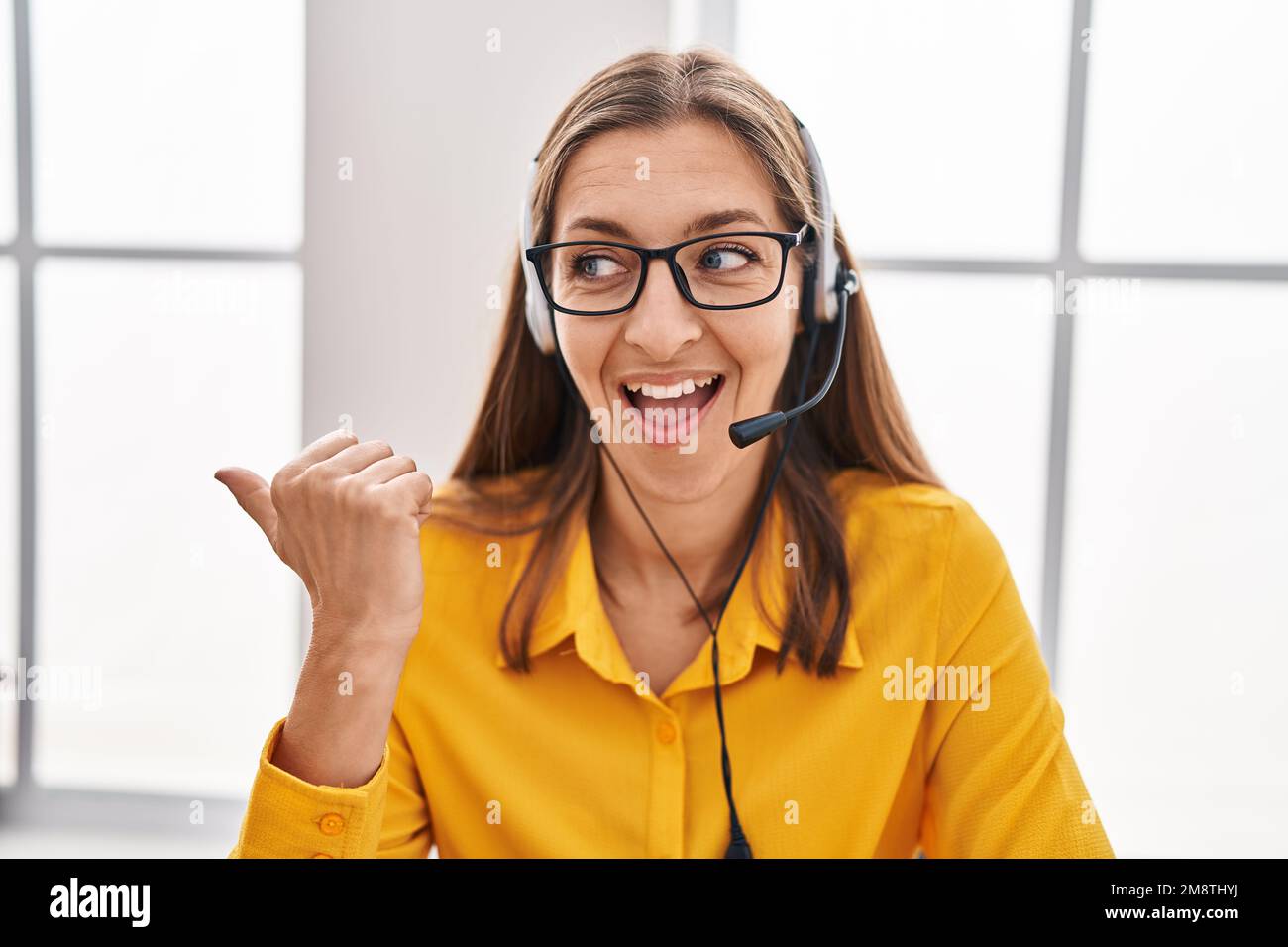 Young woman wearing call center agent headset pointing thumb up to the ...