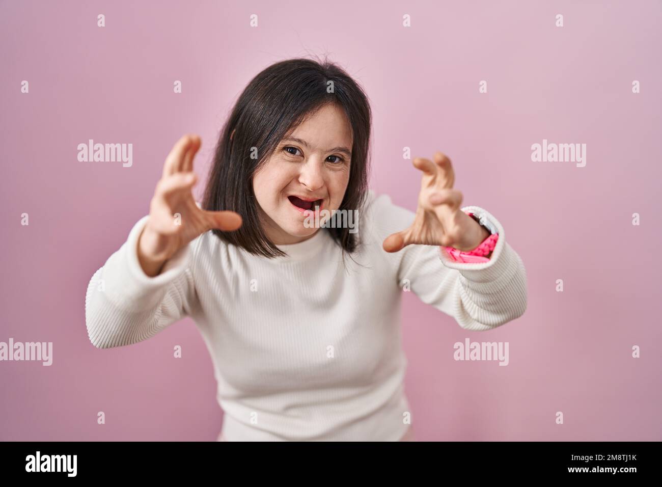 Woman with down syndrome standing over pink background shouting ...