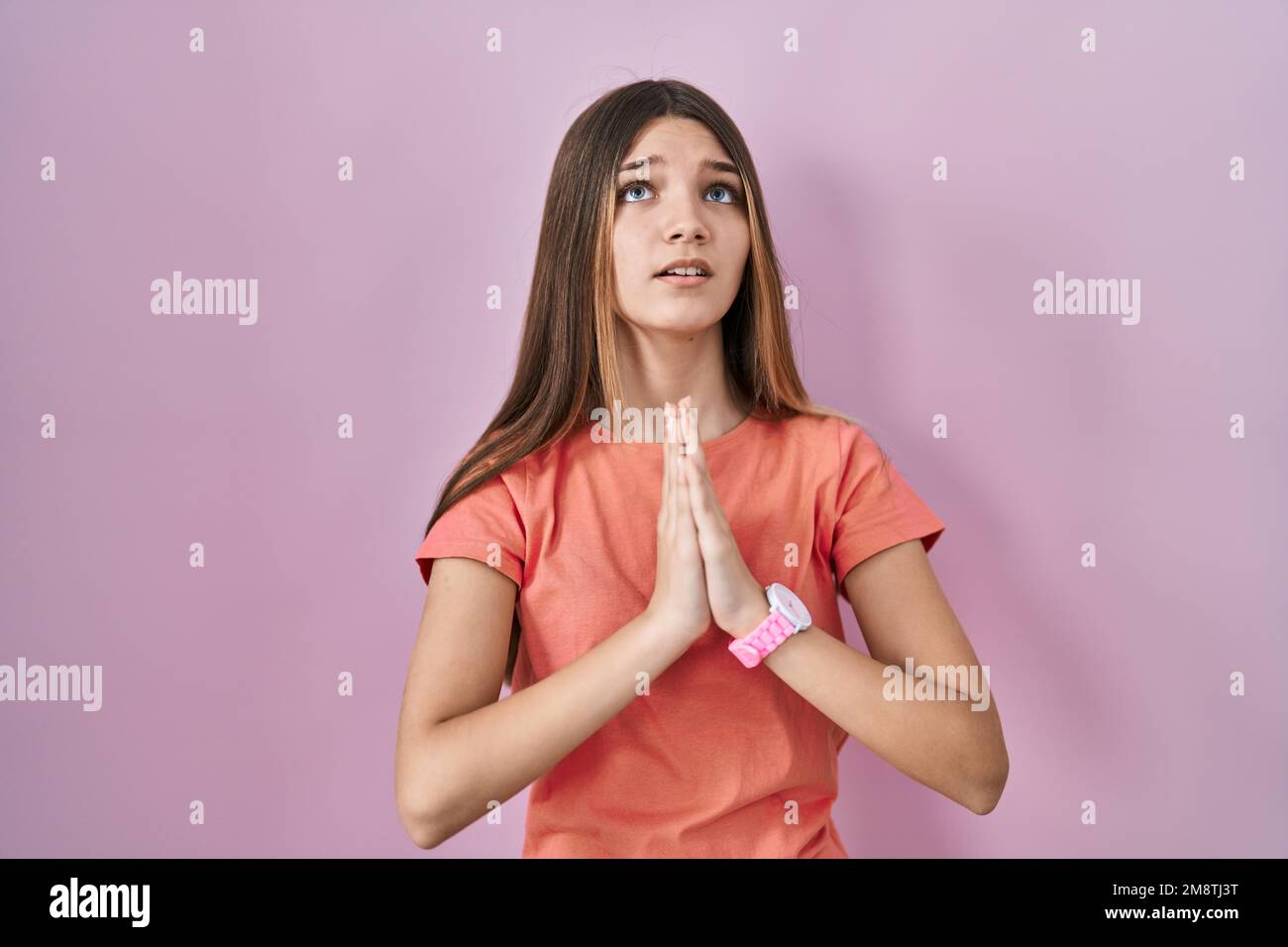 Teenager girl standing over pink background begging and praying with ...