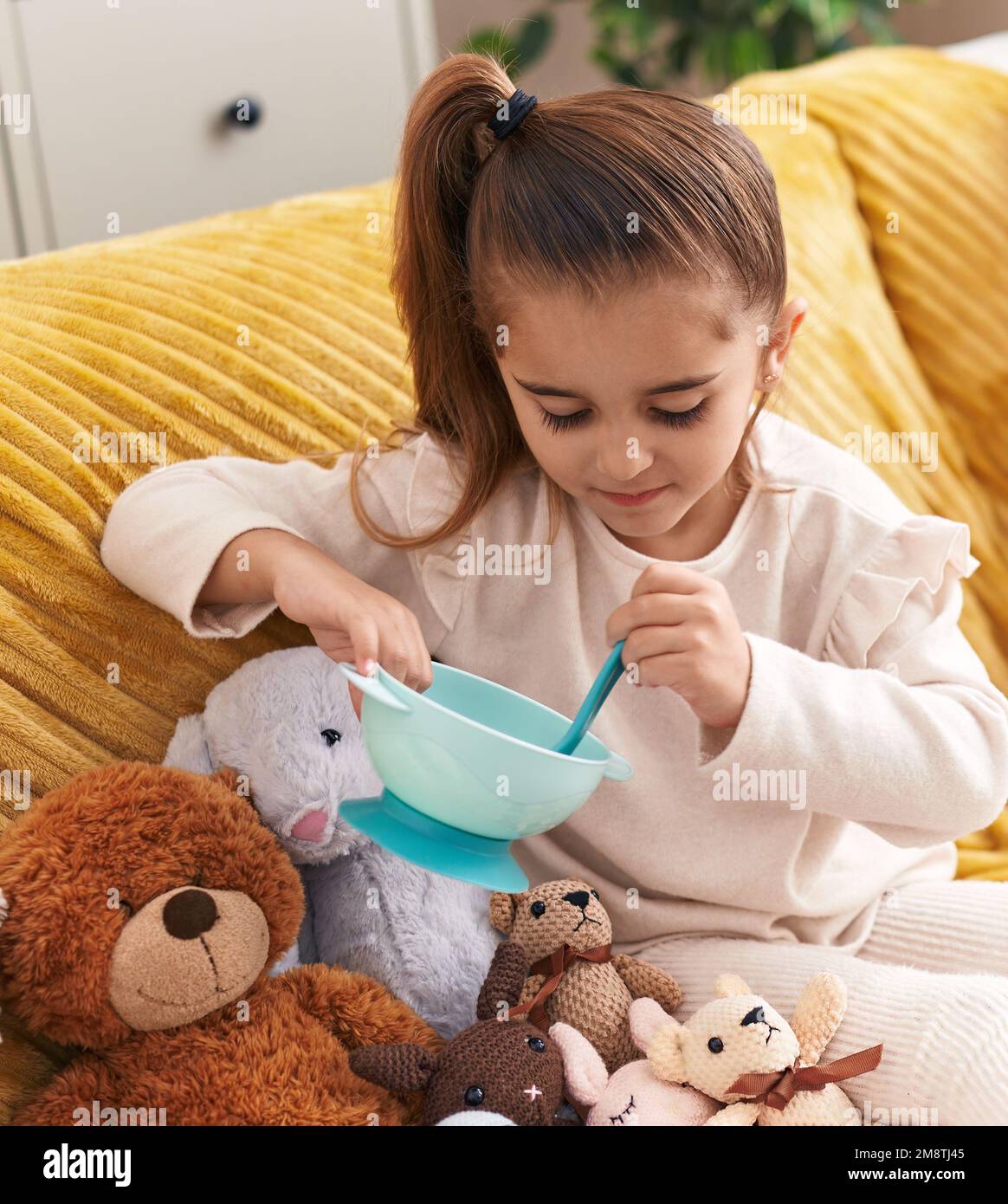 Adorable hispanic girl sitting on sofa eating at home Stock Photo - Alamy