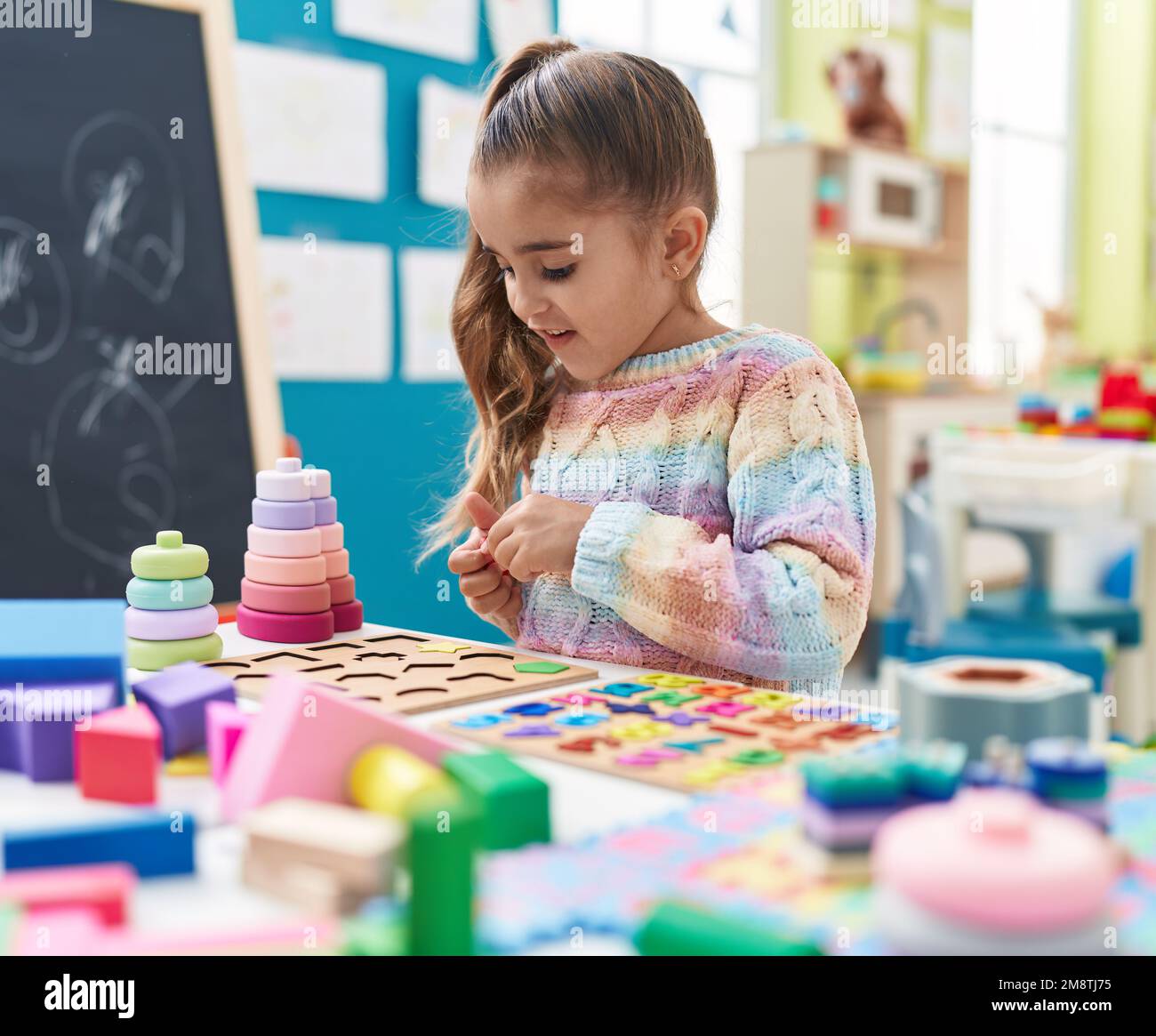 Adorable hispanic girl playing with maths puzzle game standing at ...