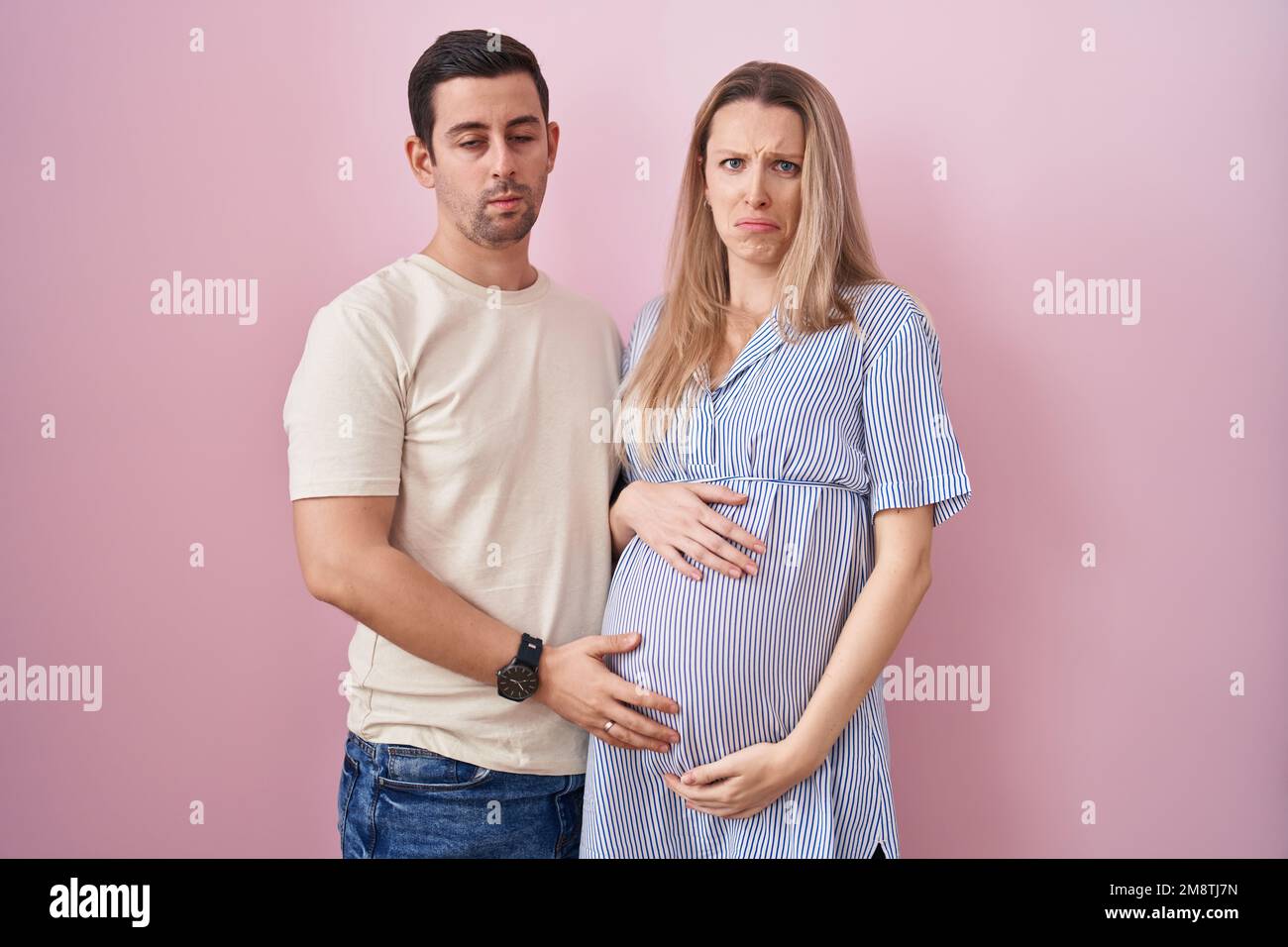 Young couple expecting a baby standing over pink background depressed ...