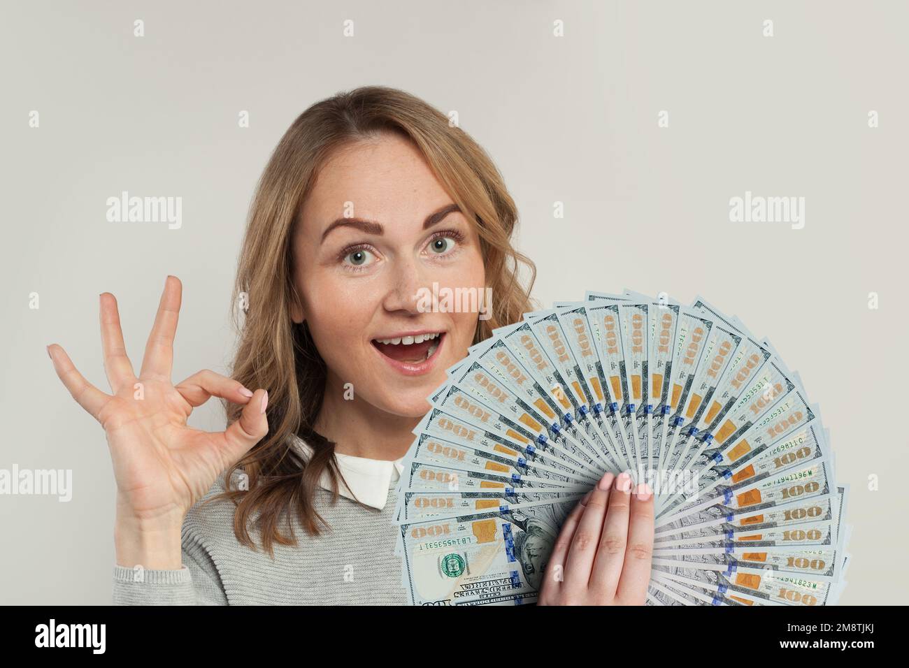 Happy woman holding fan of us dollars money showing ok sign on white ...