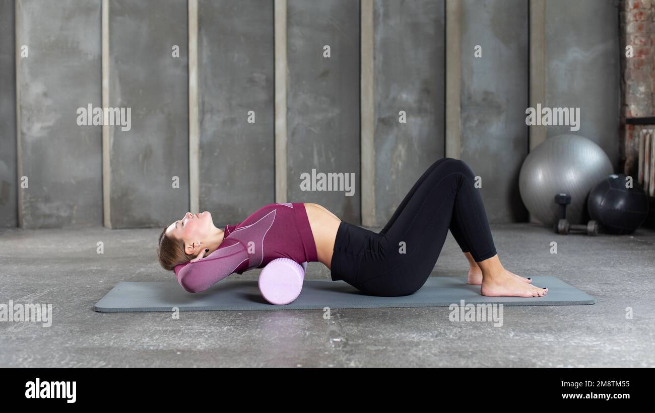 A woman performs a myofascial release for her back using a roll on a ...