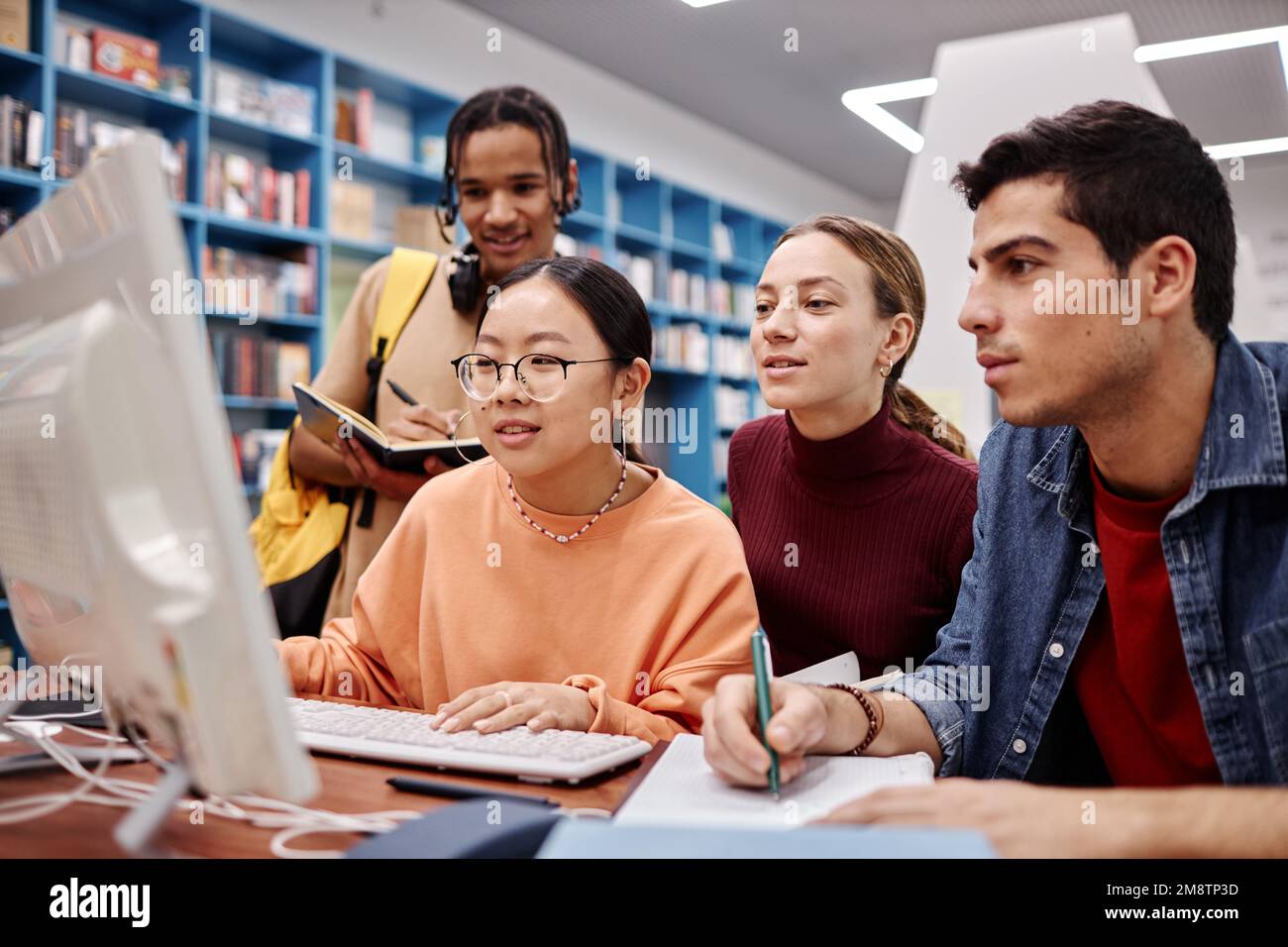 Diverse group of college students in library, focus on Asian girl using ...