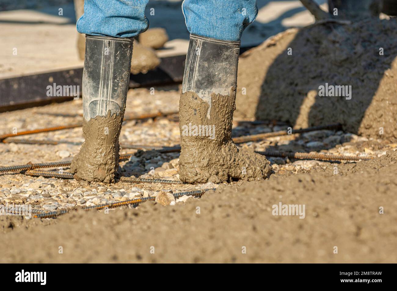 A worker's boots are covered in wet concrete while pouring a reinforced ...