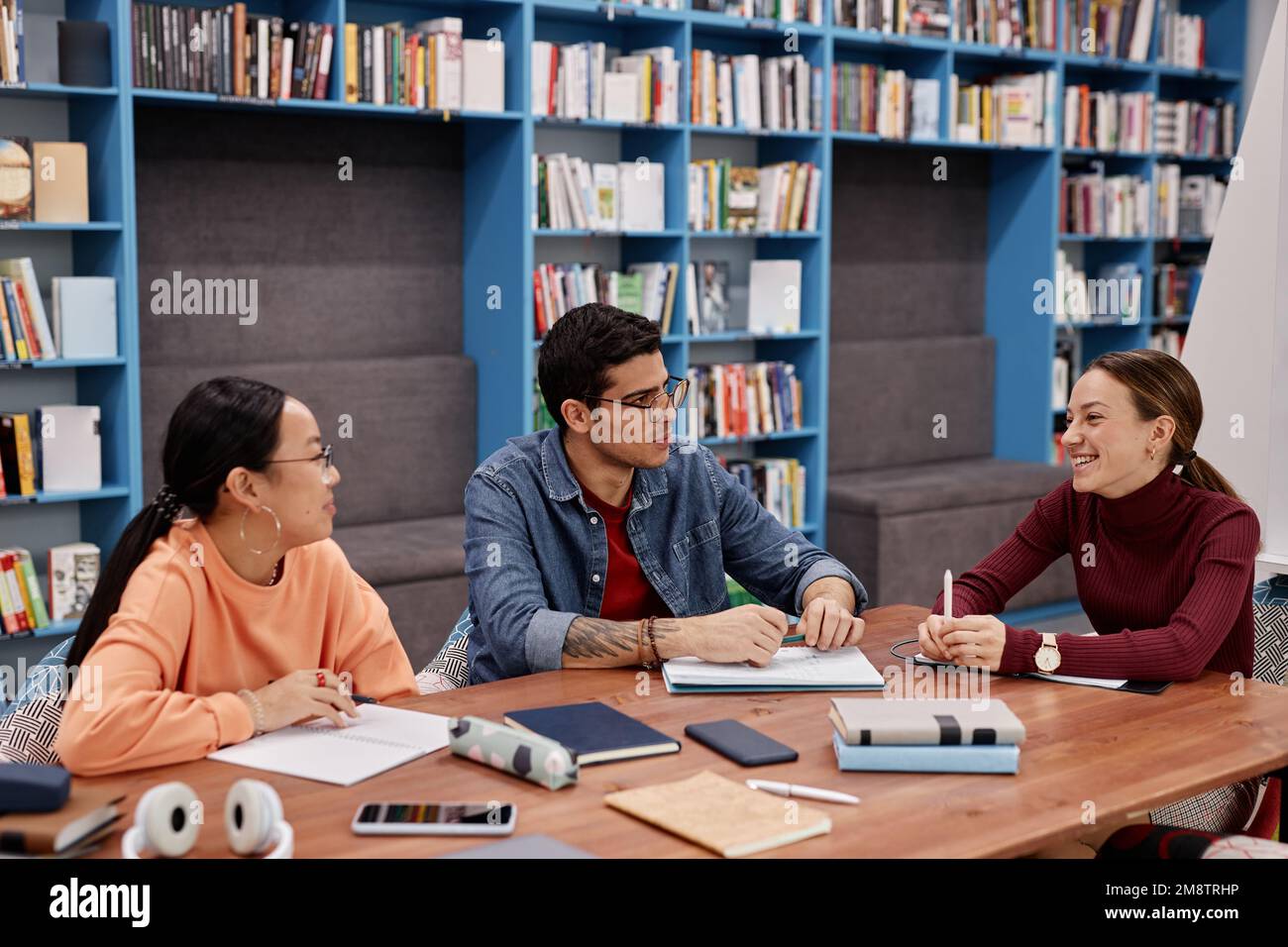 Group of three young people studying together at table in modern college library interior Stock ...