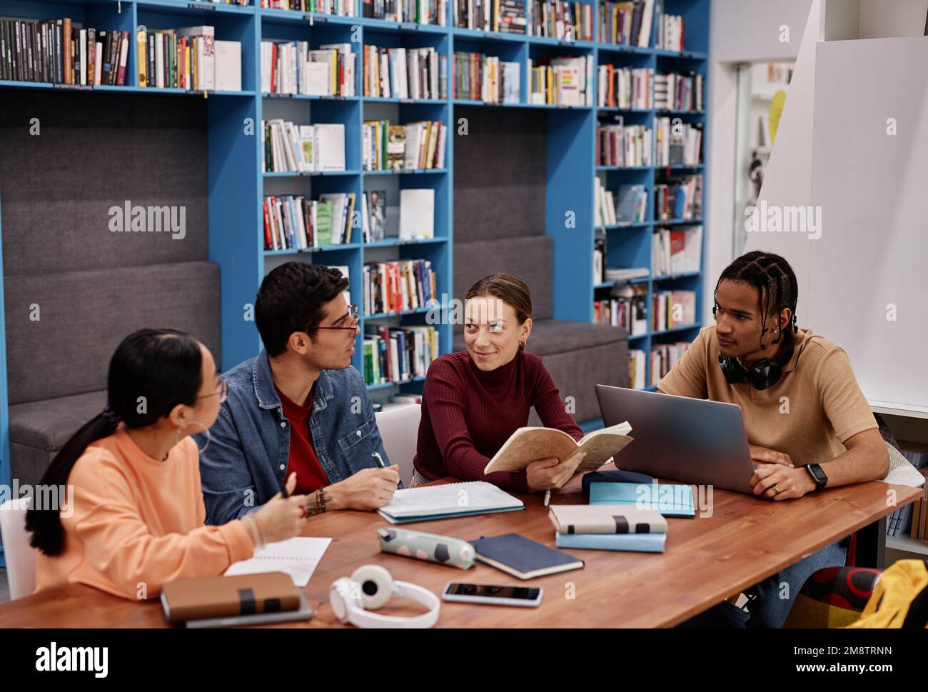 Diverse group of young people studying together sitting at table in ...