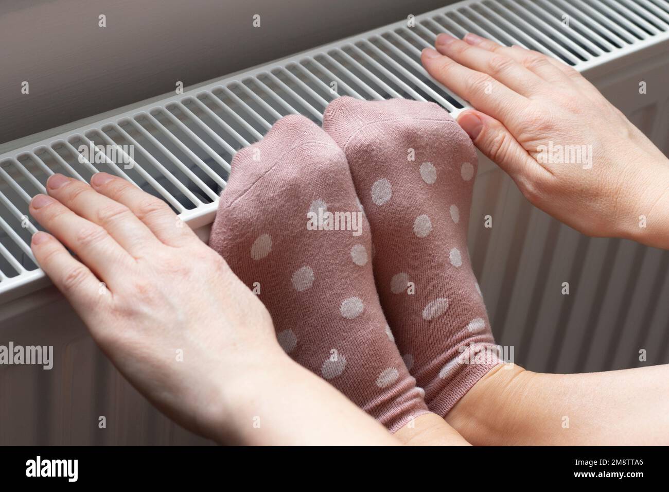 A woman warms her feet and hands in socks on a radiator. Home heating ...