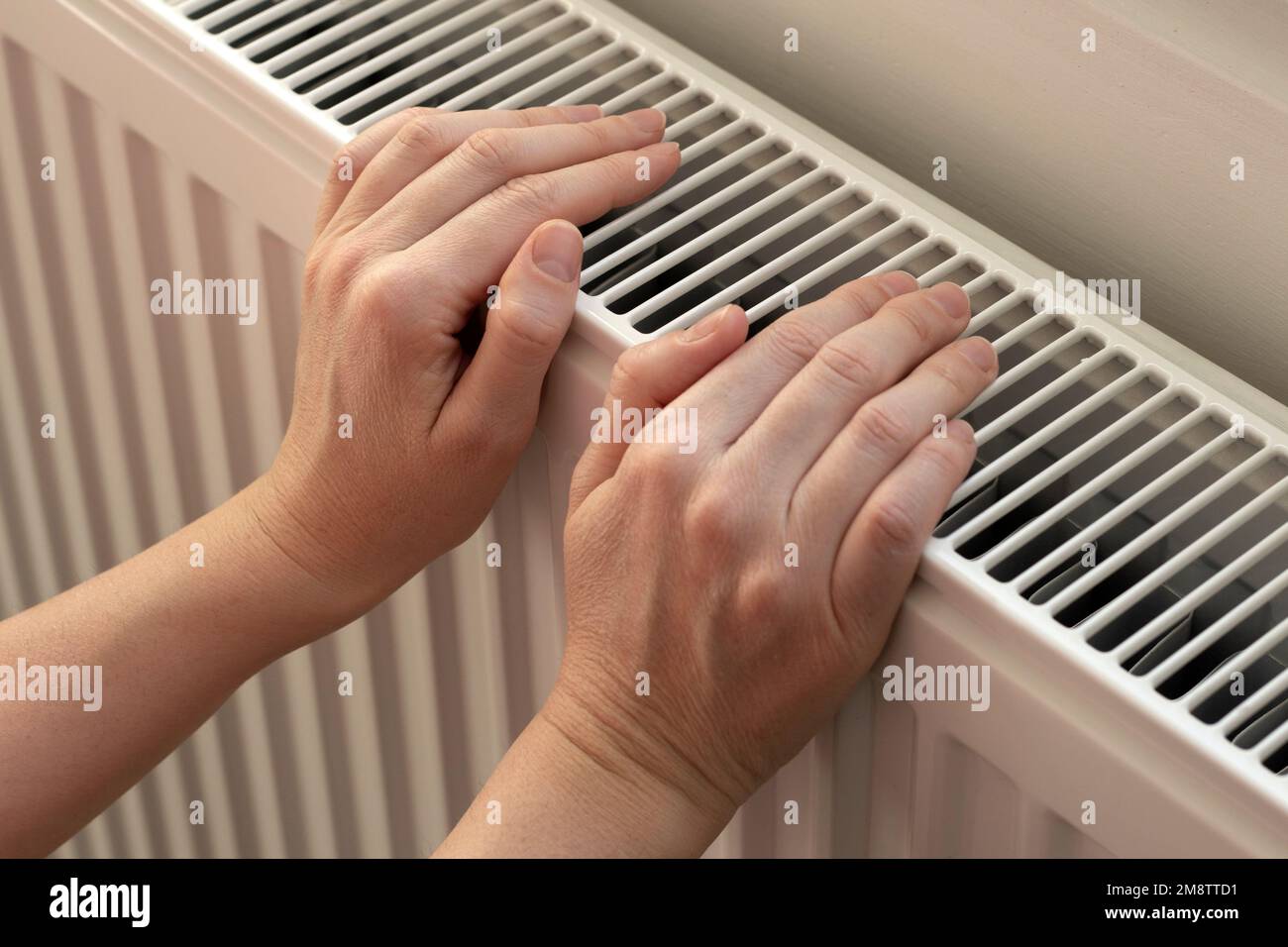 A woman warms hands on a radiator. Home heating. Low temperature and ...
