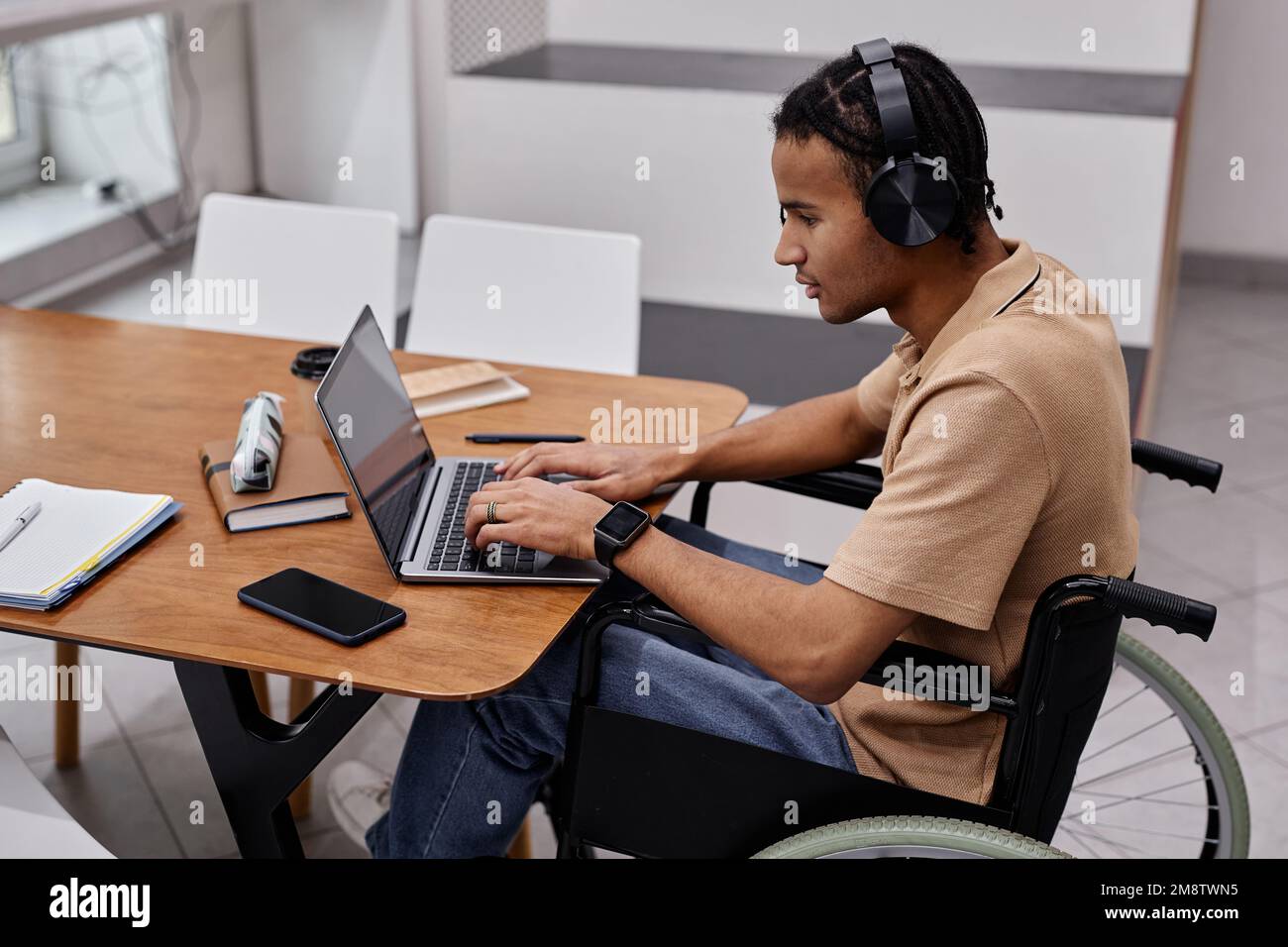 Portrait of black young man with disability using laptop in college ...