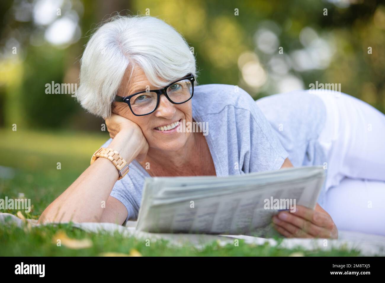 senior woman reading newspaper laying in the grass Stock Photo - Alamy