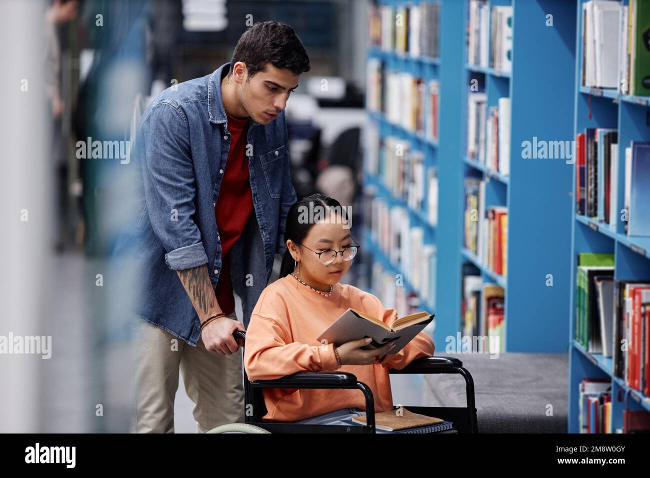 Portrait of Asian girl with disability in library choosing books with ...