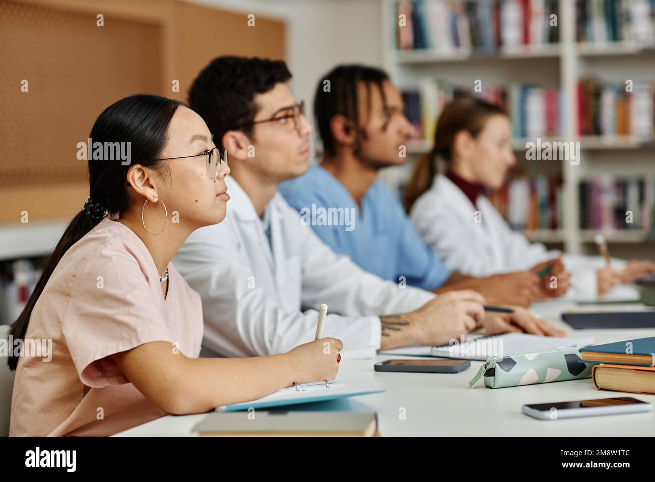 Side view portrait of young people sitting in row at table and ...
