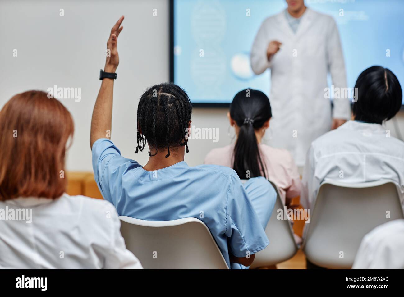 Back view at young black doctor raising hand in audience at medical ...