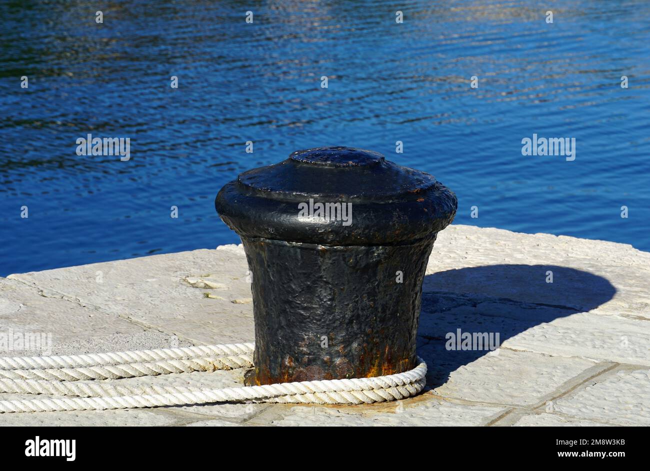 A black metal pole for mooring ships wrapped in a white thick rope in a ...