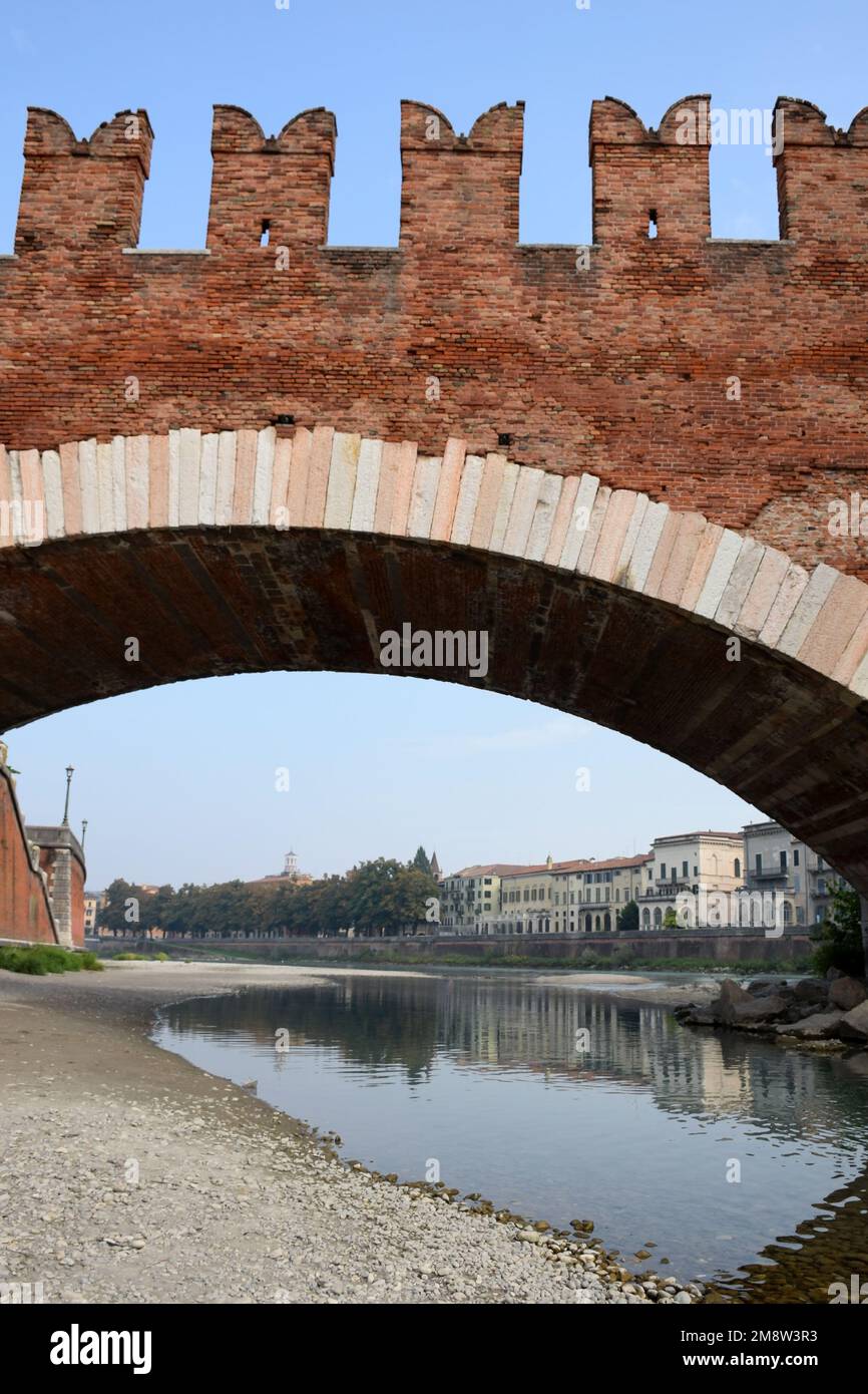Medieval stone bridge over a shallow river made of red brick. Below it ...