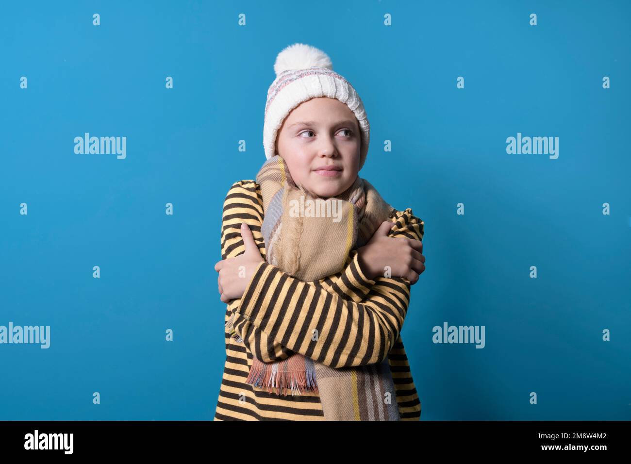 A teenage girl is freezing in the cold. Studio portrait. Blue ...
