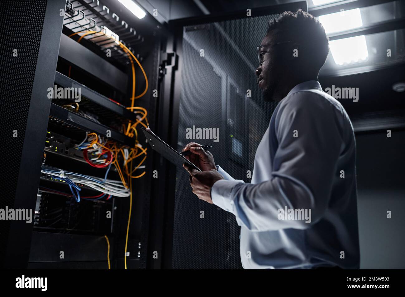 Backlit side view portrait of black man working with server cabinet in ...