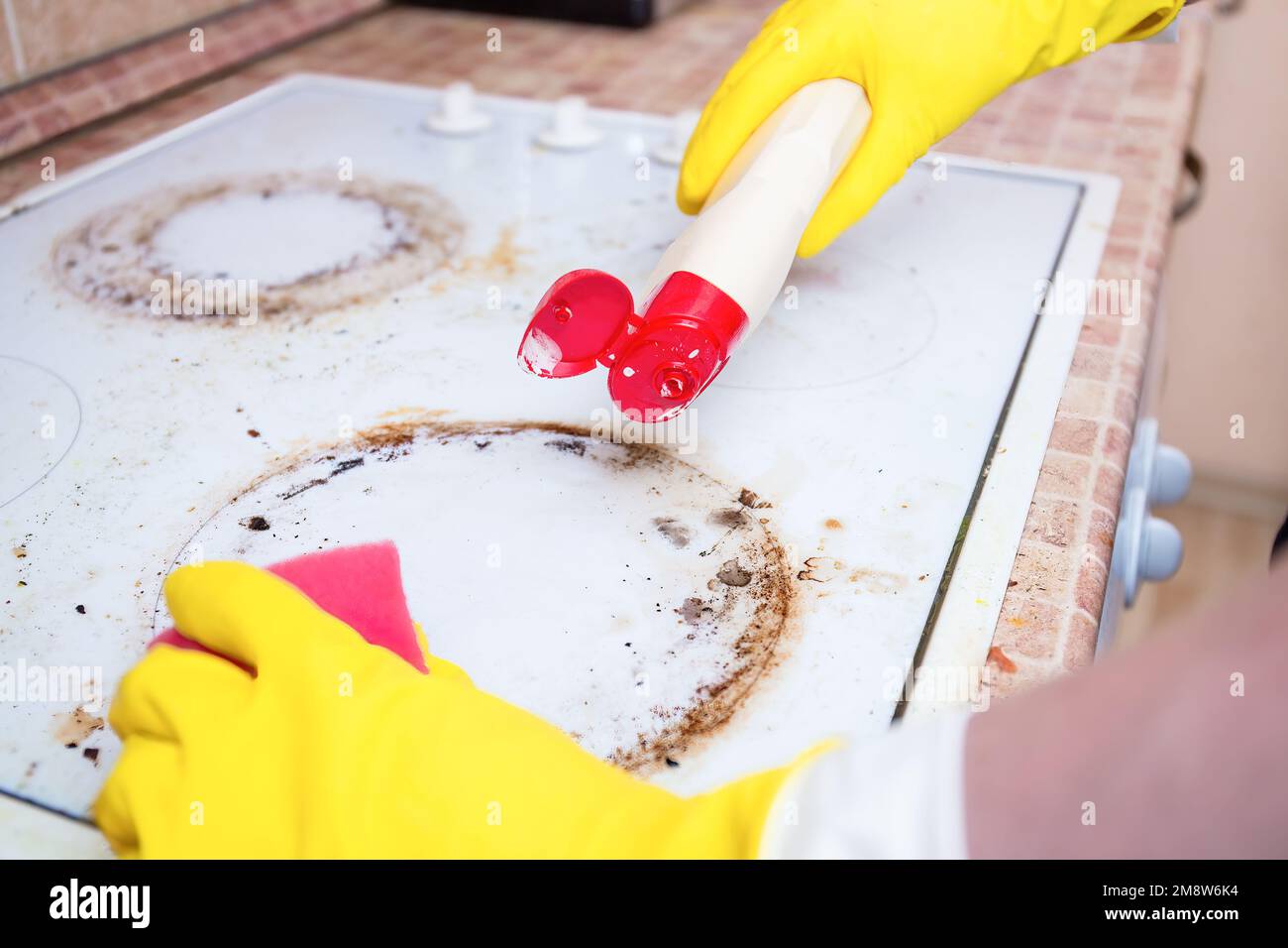Man cleaning ceramic modern stove or hob with detergent agent. Hand in ...