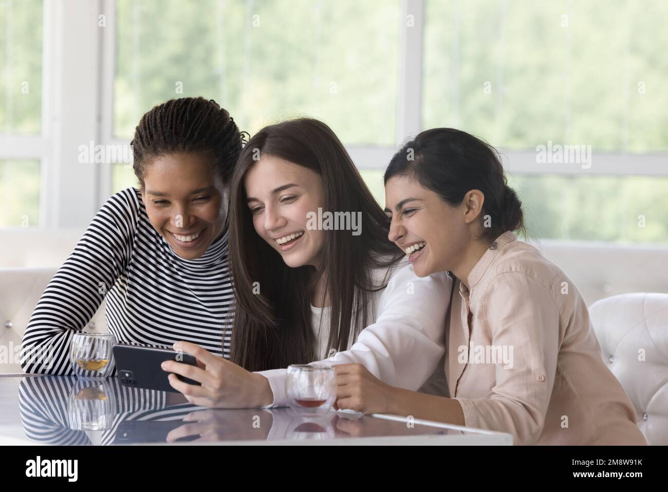 Three cheerful diverse girls making group video call on smartphone ...