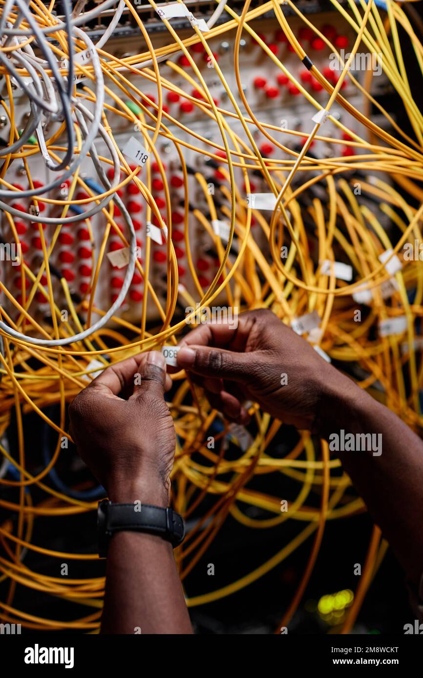 Vertical close up of male hands connecting cables and wires in server room while setting up ...