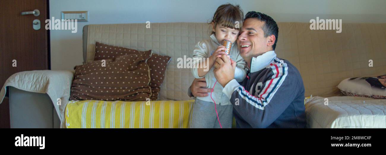 Image of a smiling dad hugging his daughter as they play house and sing ...