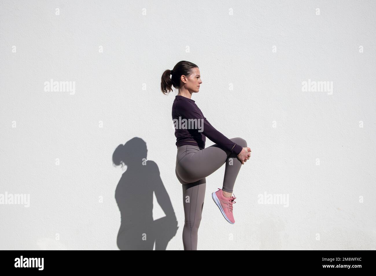 fit sporty woman doing leg stretching exercises outside against a white ...