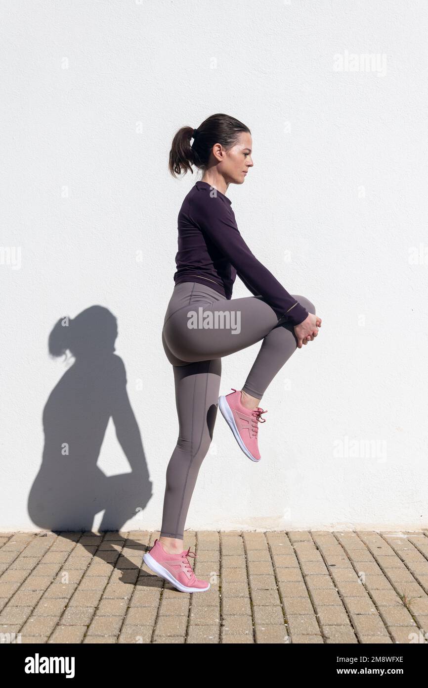 fit sporty woman doing leg stretching exercises outside against a white ...