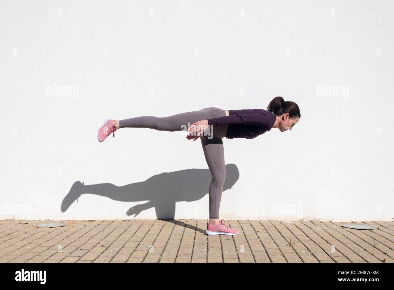 Sporty woman doing warrior three yoga pose against a white wall in the ...