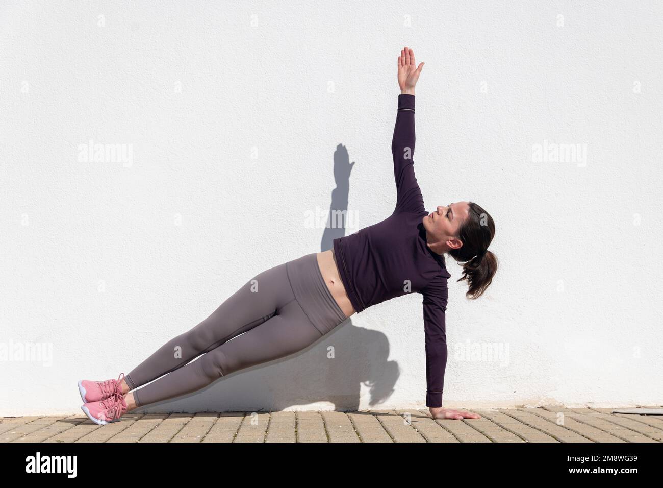sporty woman doing a side plank exercise outside against a white wall ...