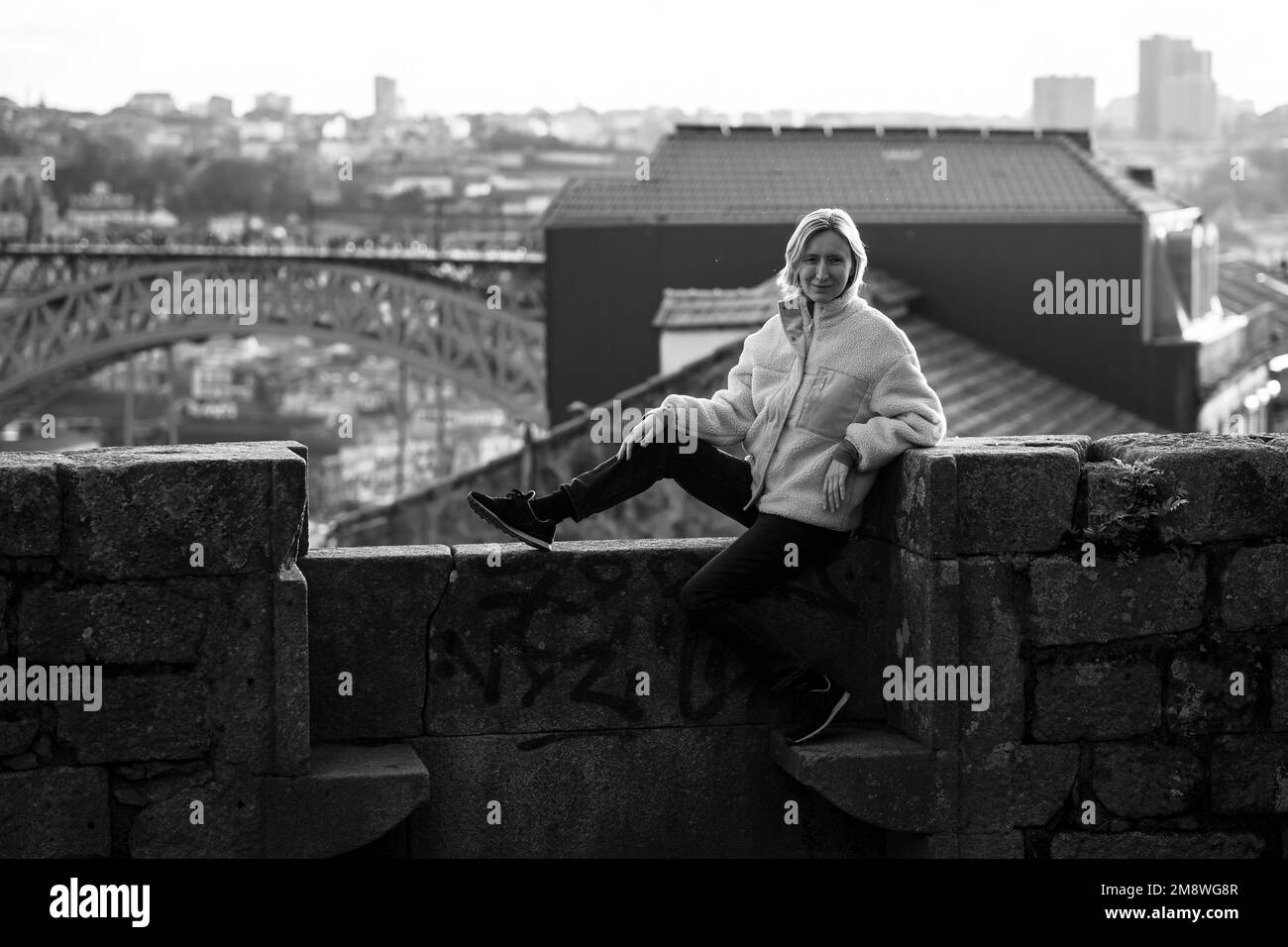 A female tourist sits on a masonry wall in Porto, Portugal. Black and ...