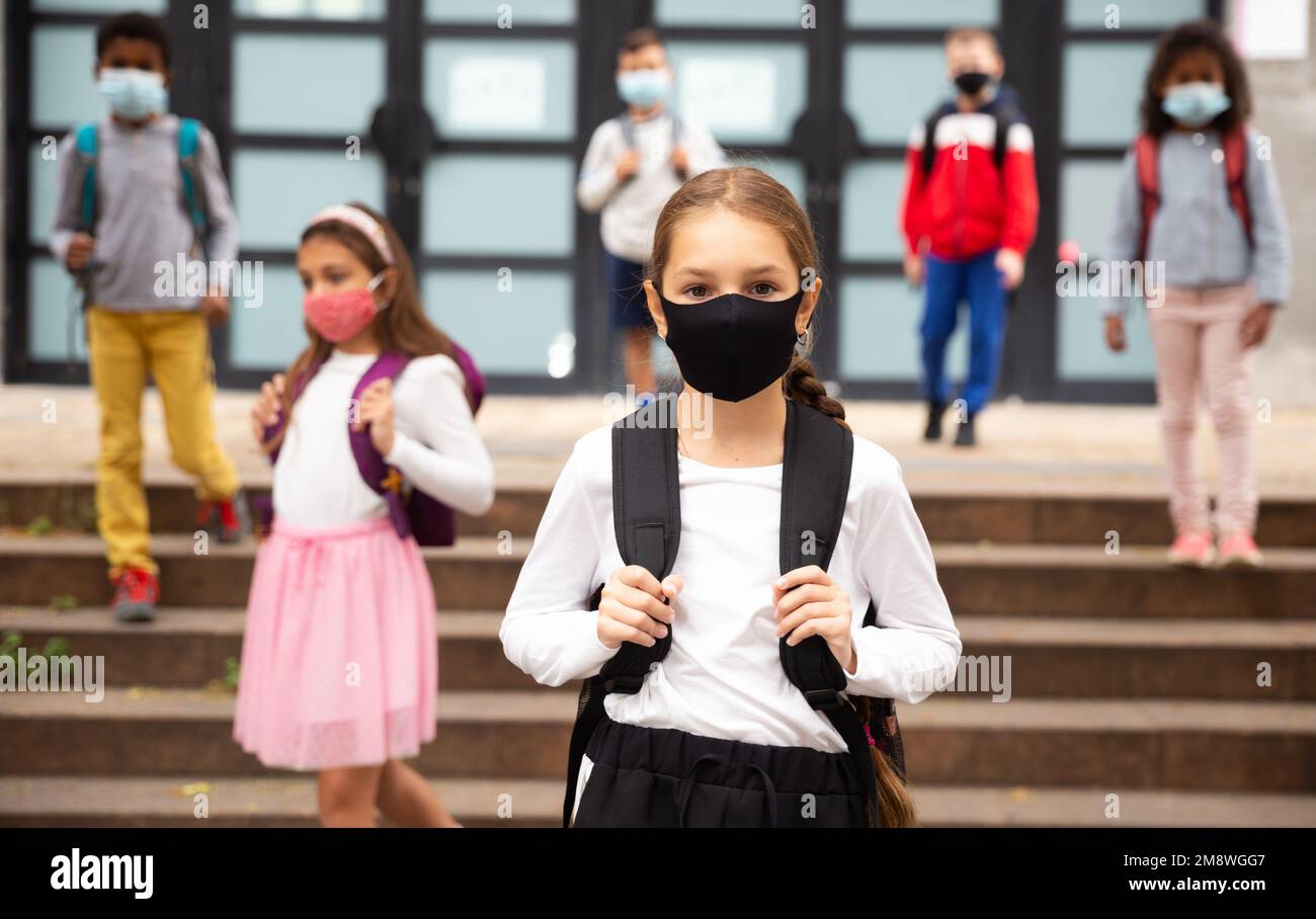 Schoolgirl in mask standing near school, children on background Stock ...
