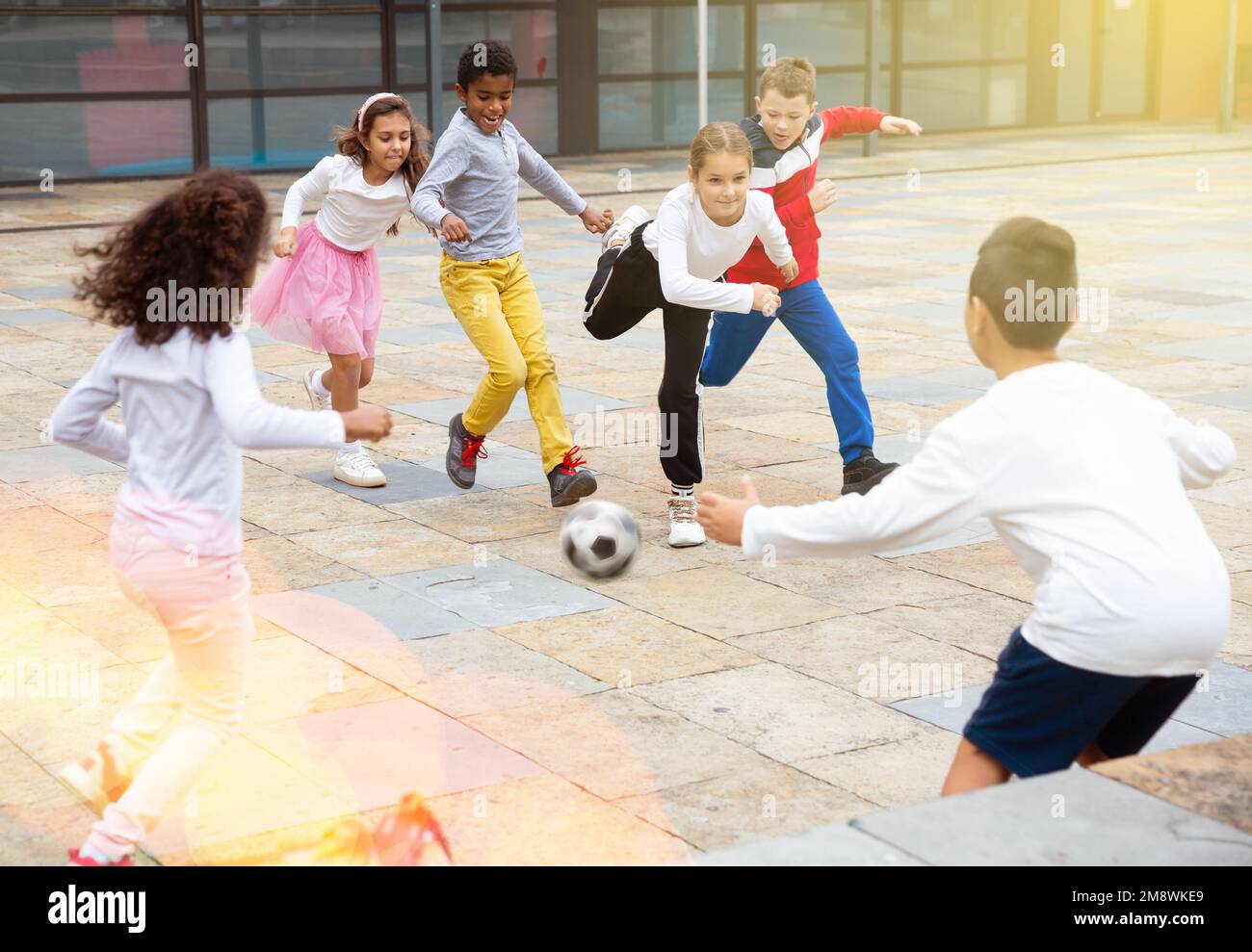 Cheerful tween schoolchildren playing with ball near school Stock Photo ...