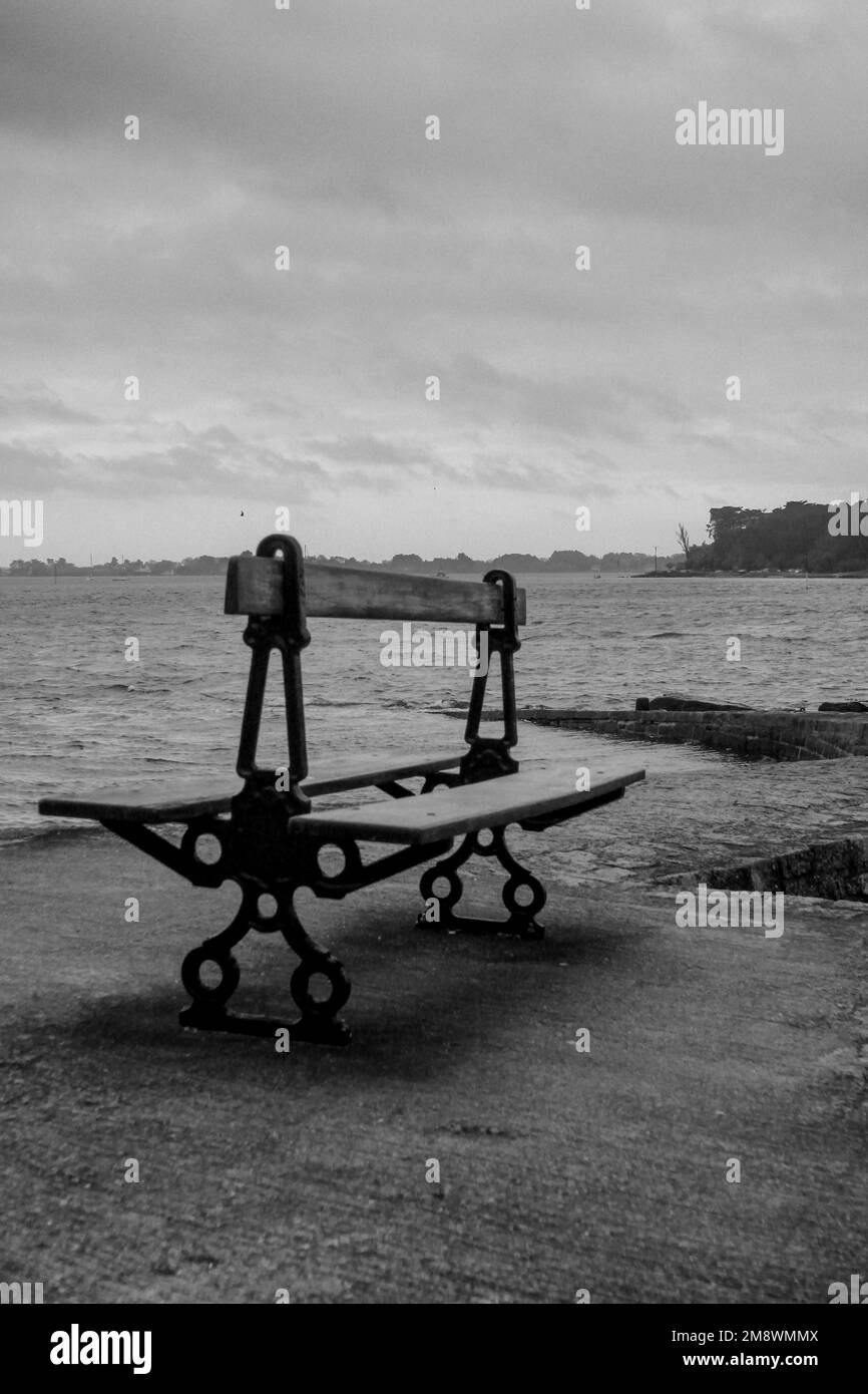 A wrought iron bench faces the ocean. Black and white photo in bad ...
