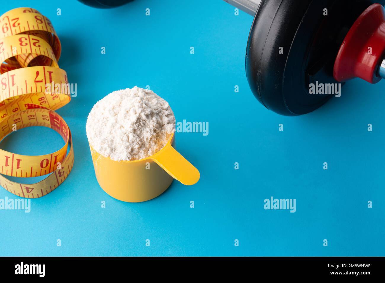 A scoop of creatine next to a dumbbell and a tape measure on a blue ...