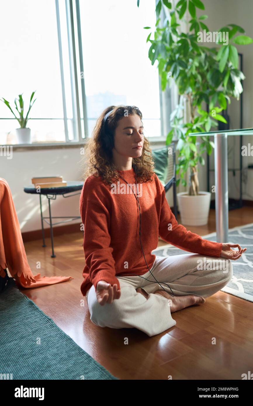 Young mindful woman wearing headphones doing meditation at home ...